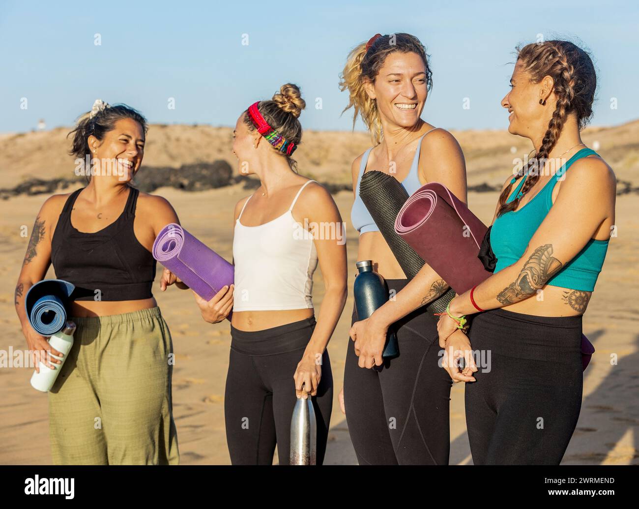 Group of happy women friends laughing and carrying yoga mats after a ...