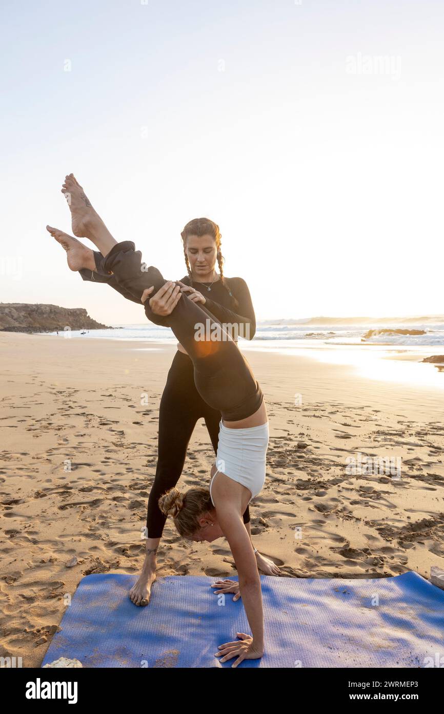 Two people engage in an acrobatic yoga pose on a beach mat at sunset ...