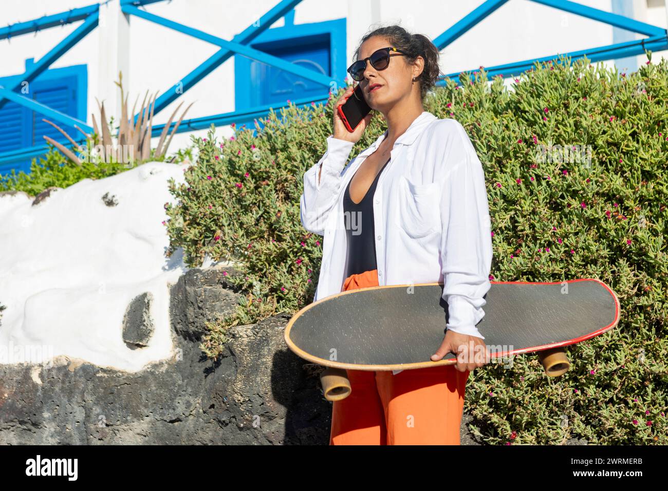 A stylish digital nomad with a skateboard chats on her phone while ...