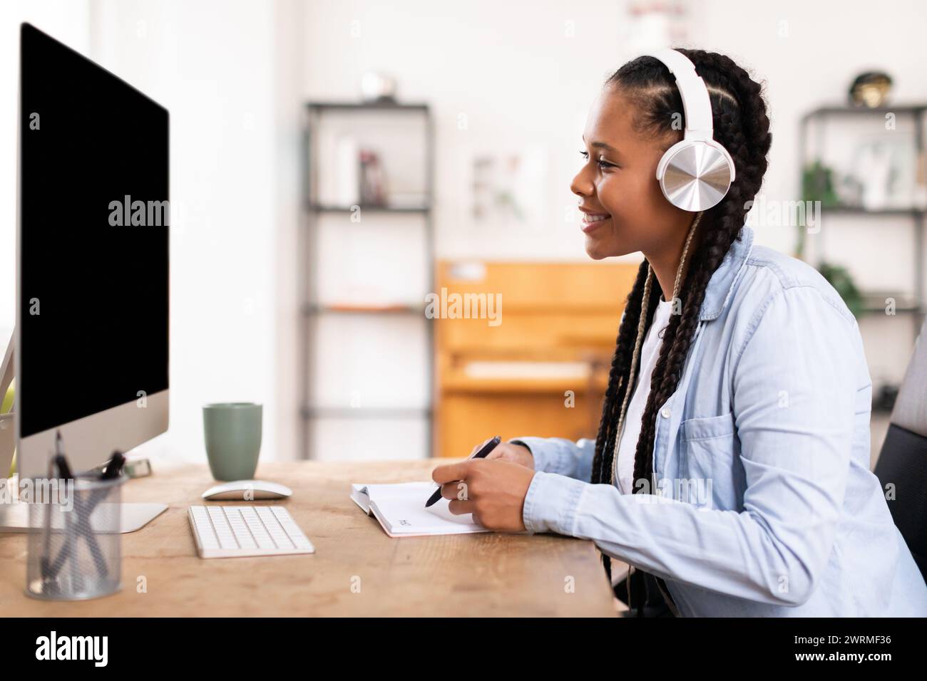 Cheerful black female student studying with headphones at computer ...