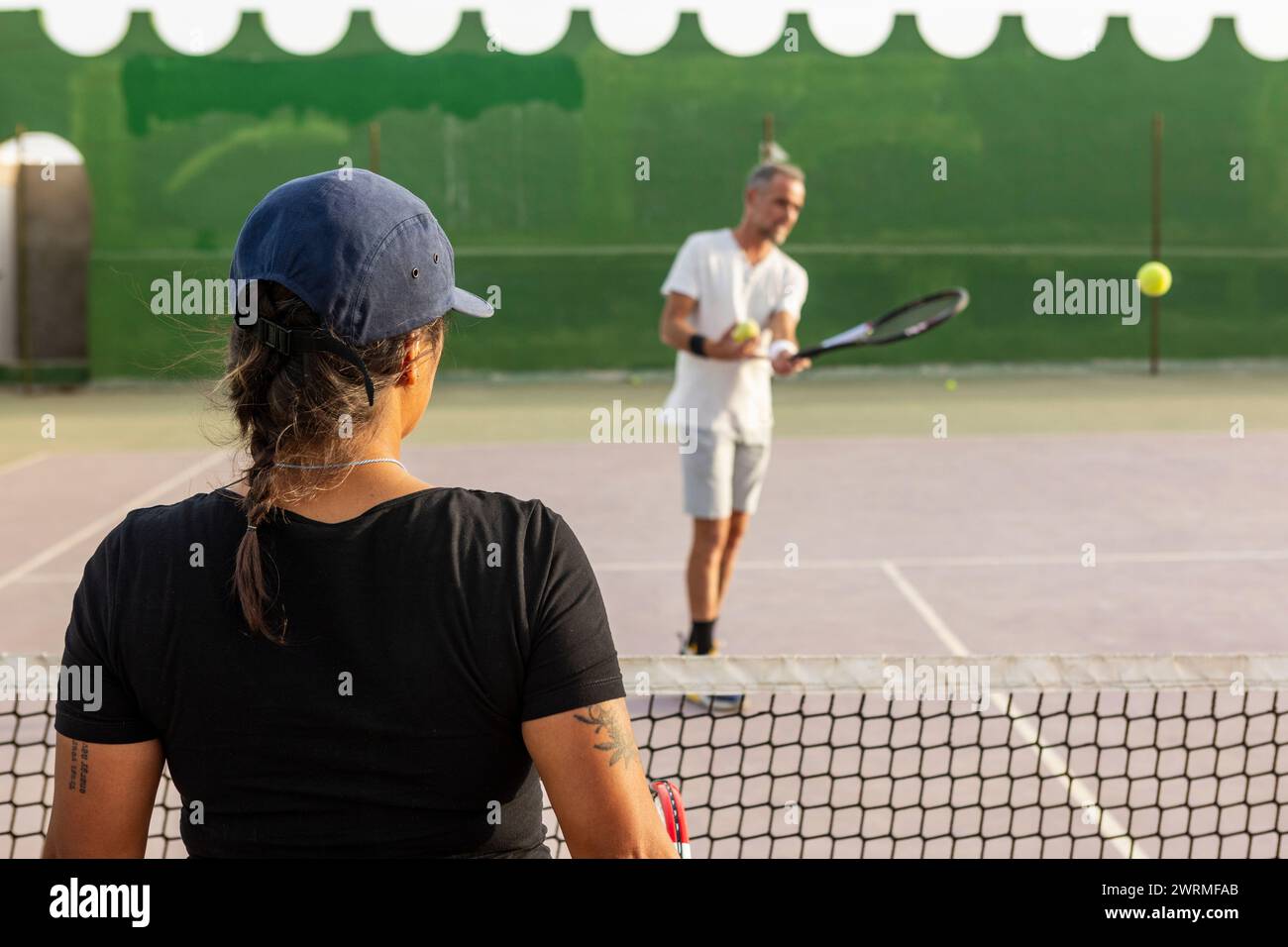 A female tennis player in a blue cap is observed from the back ...
