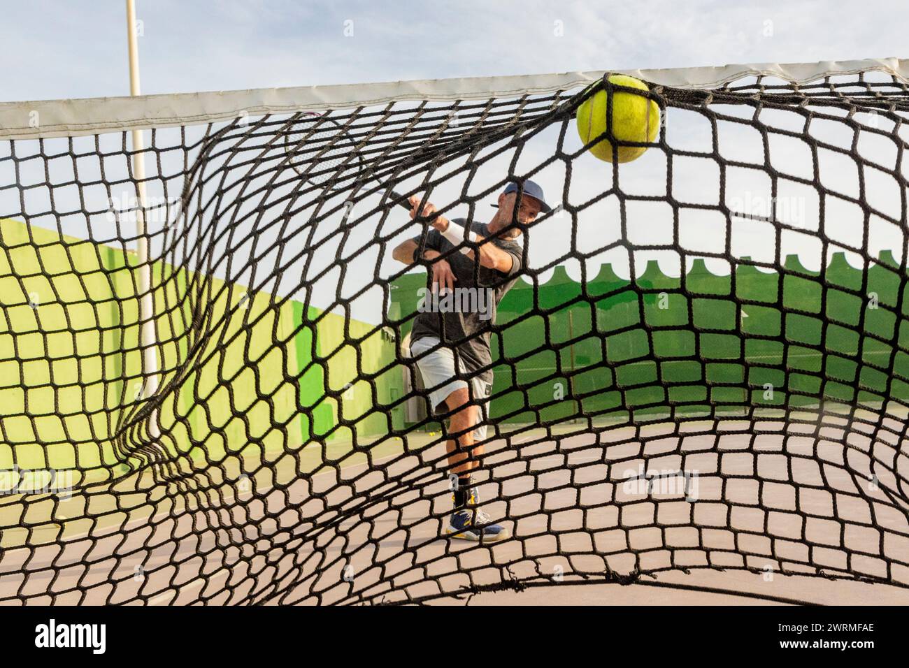 A man plays tennis viewed through the net, with a dynamic backhand stroke Stock Photo - Alamy