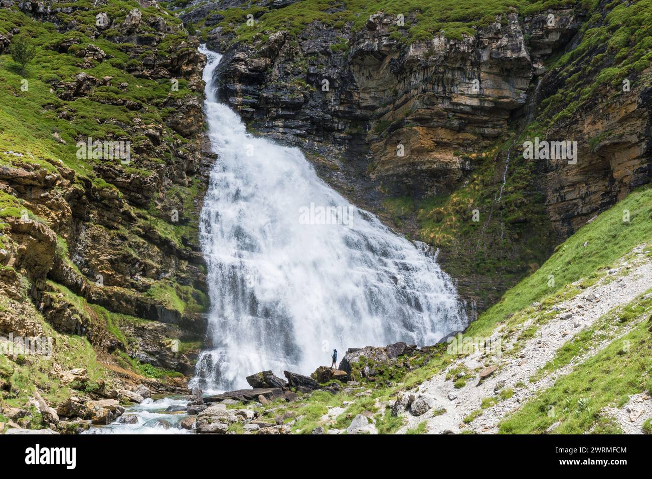 A hiker stands by a roaring waterfall in the Ordesa Valley, showcasing ...