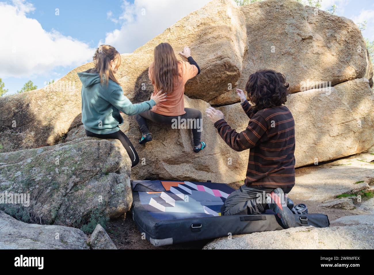 Back view of three friends engage in bouldering on a large rock, with ...