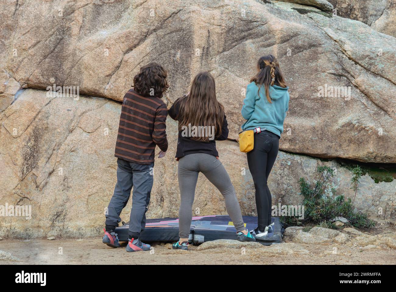 Back view of three climbers stand before a large boulder, contemplating ...