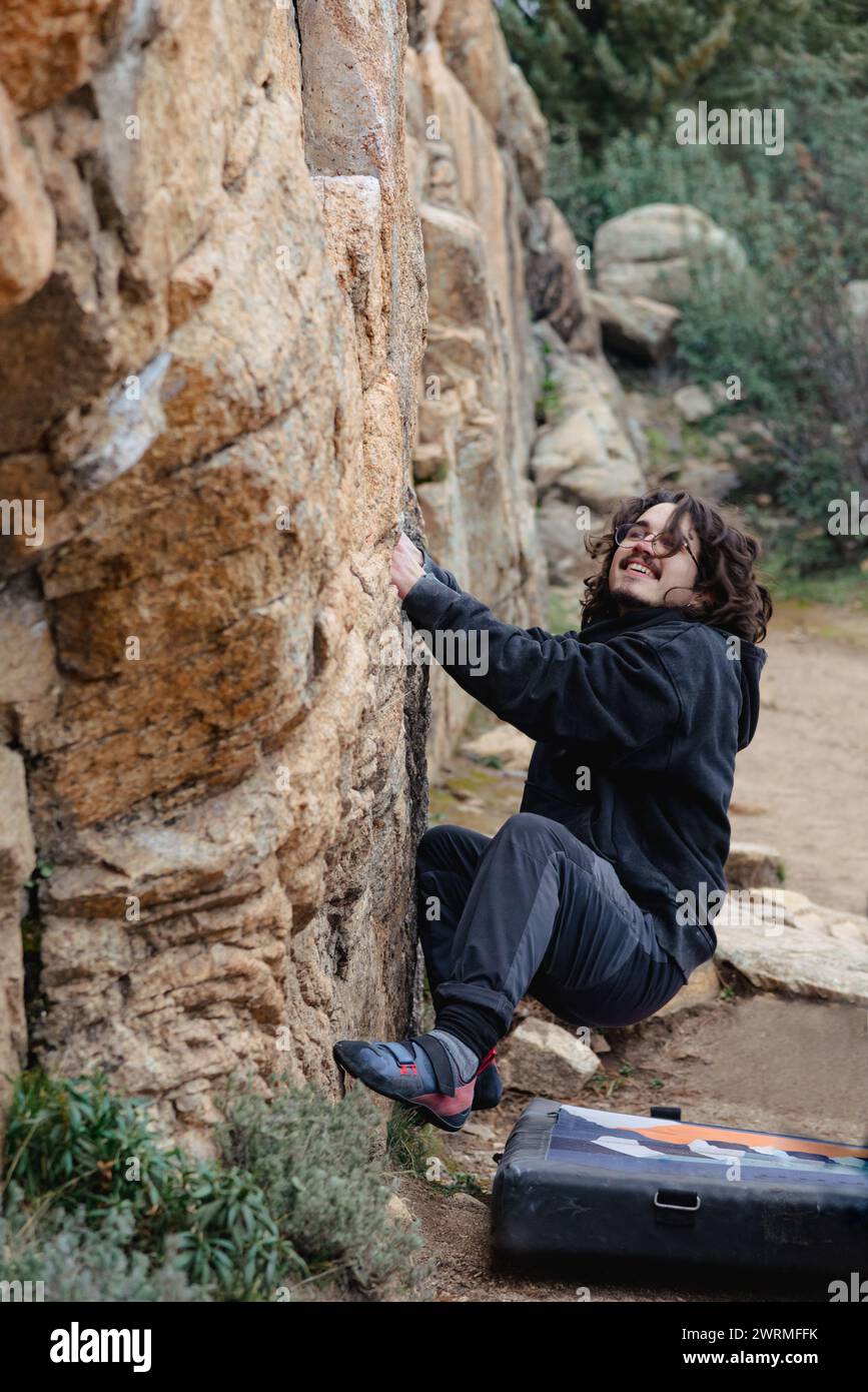A climber with curly hair engages in a challenging boulder problem ...