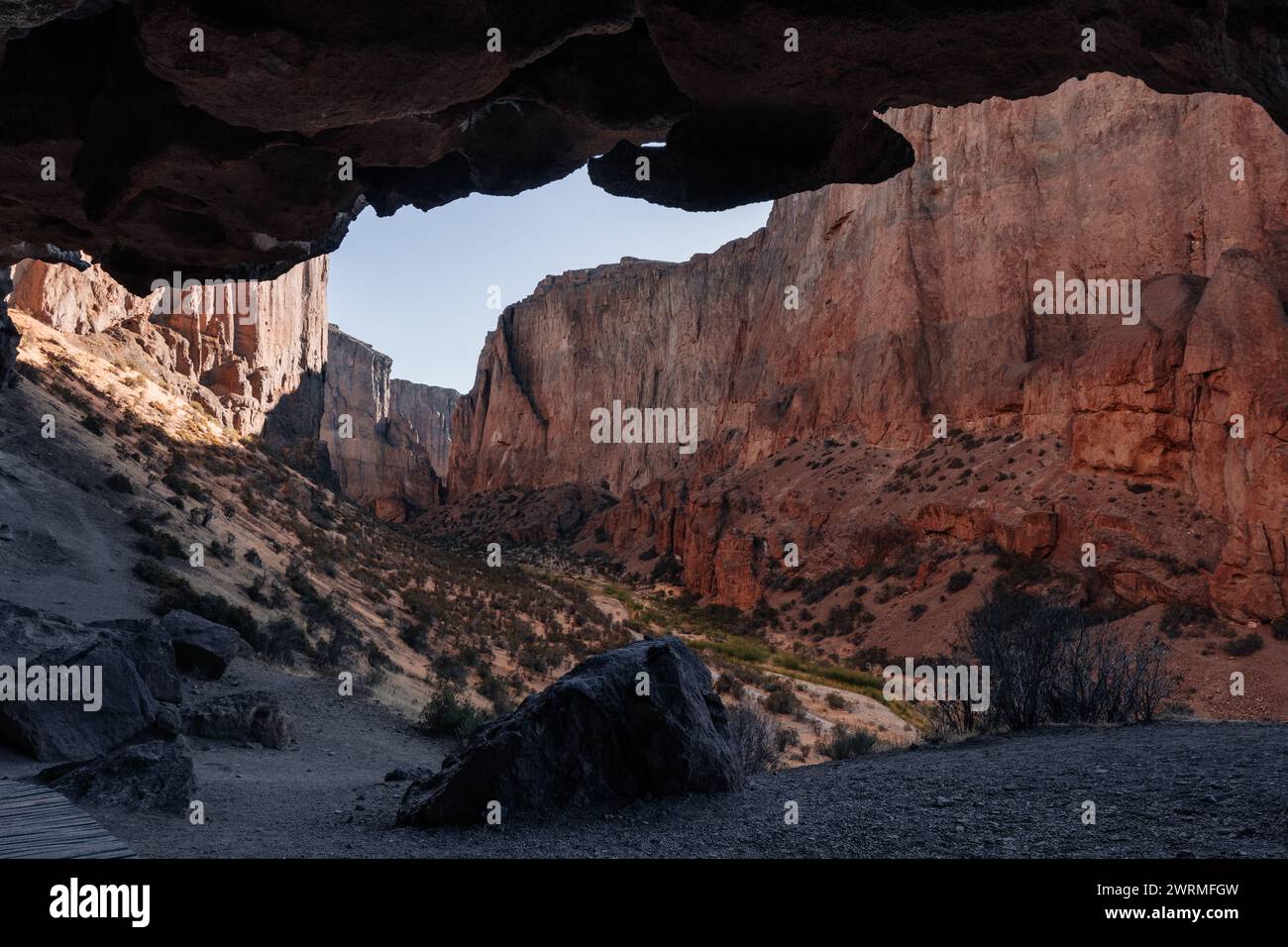 View from the shadowed interior of a cave framing the sunlit red cliffs ...