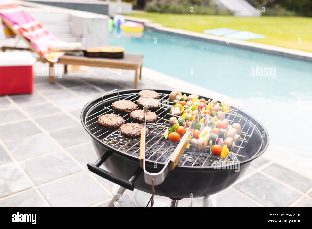 A barbecue grill is loaded with burgers and vegetable skewers, with a ...