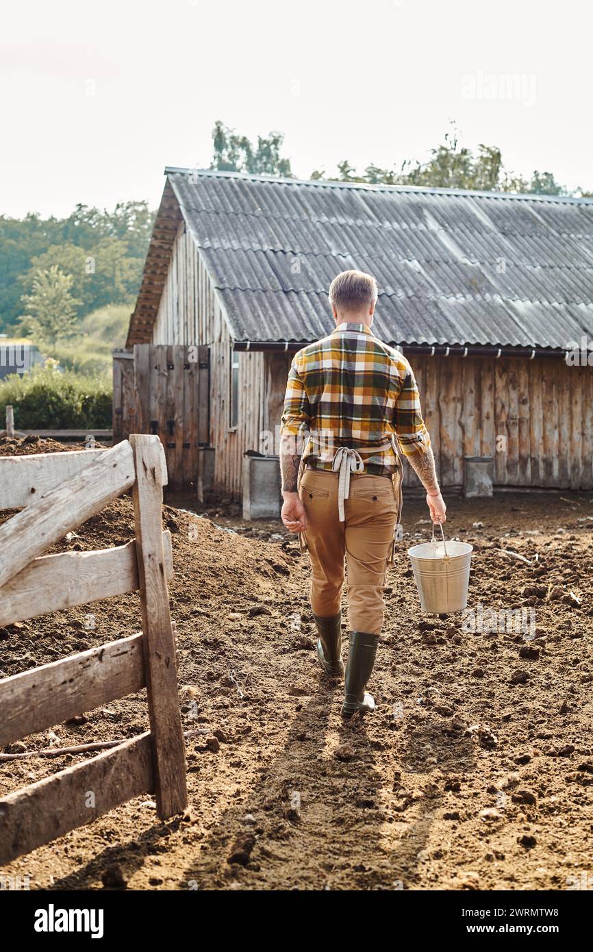 back view of adult hardworking man with tattoos on arms holding bucket ...