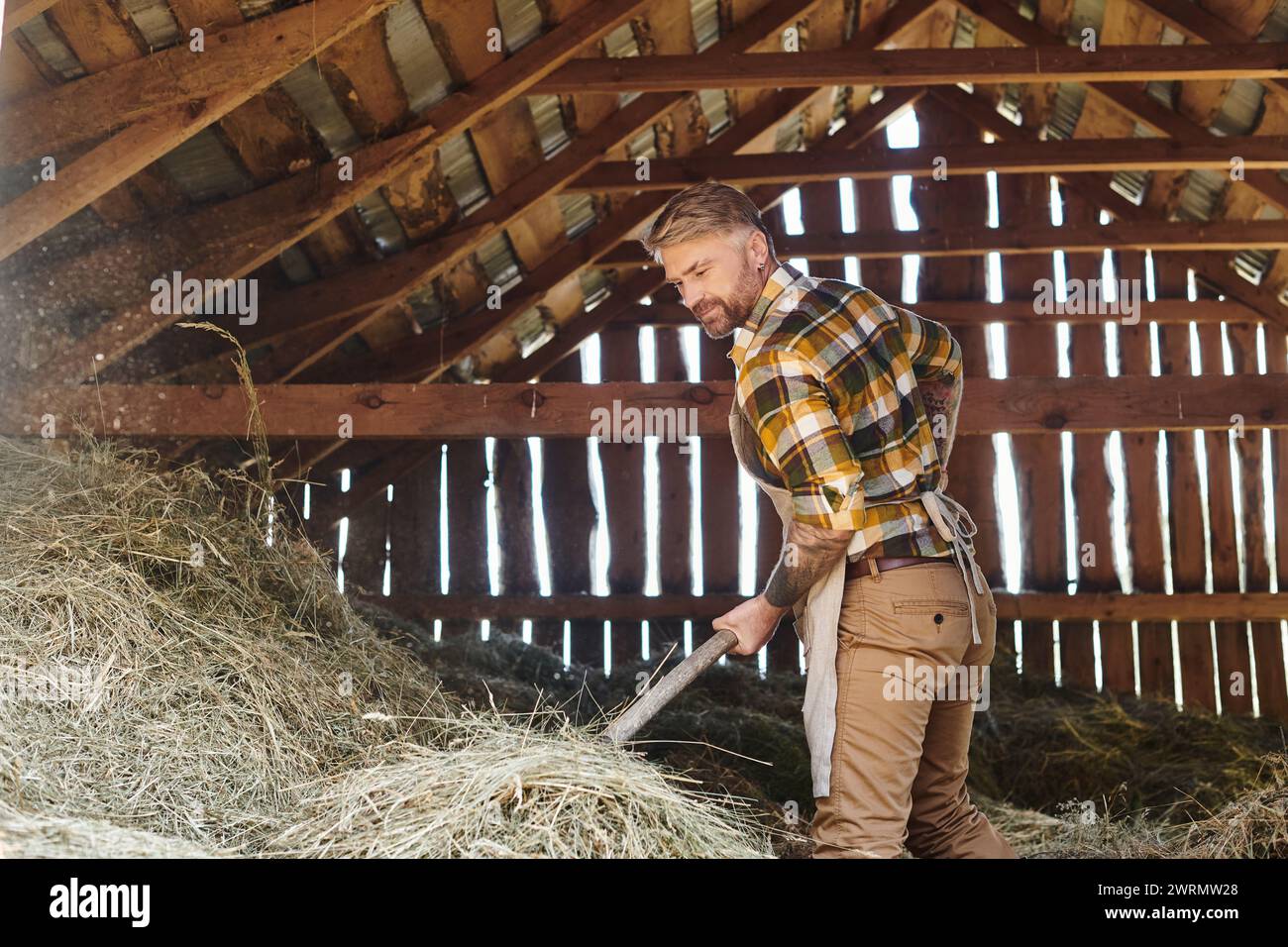 cheerful good looking man with tattoos using pitchfork while working ...