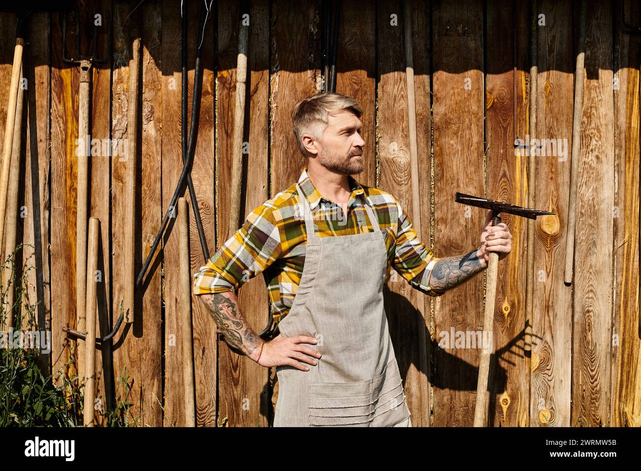 handsome dedicated farmer in casual attire using pitchfork while ...