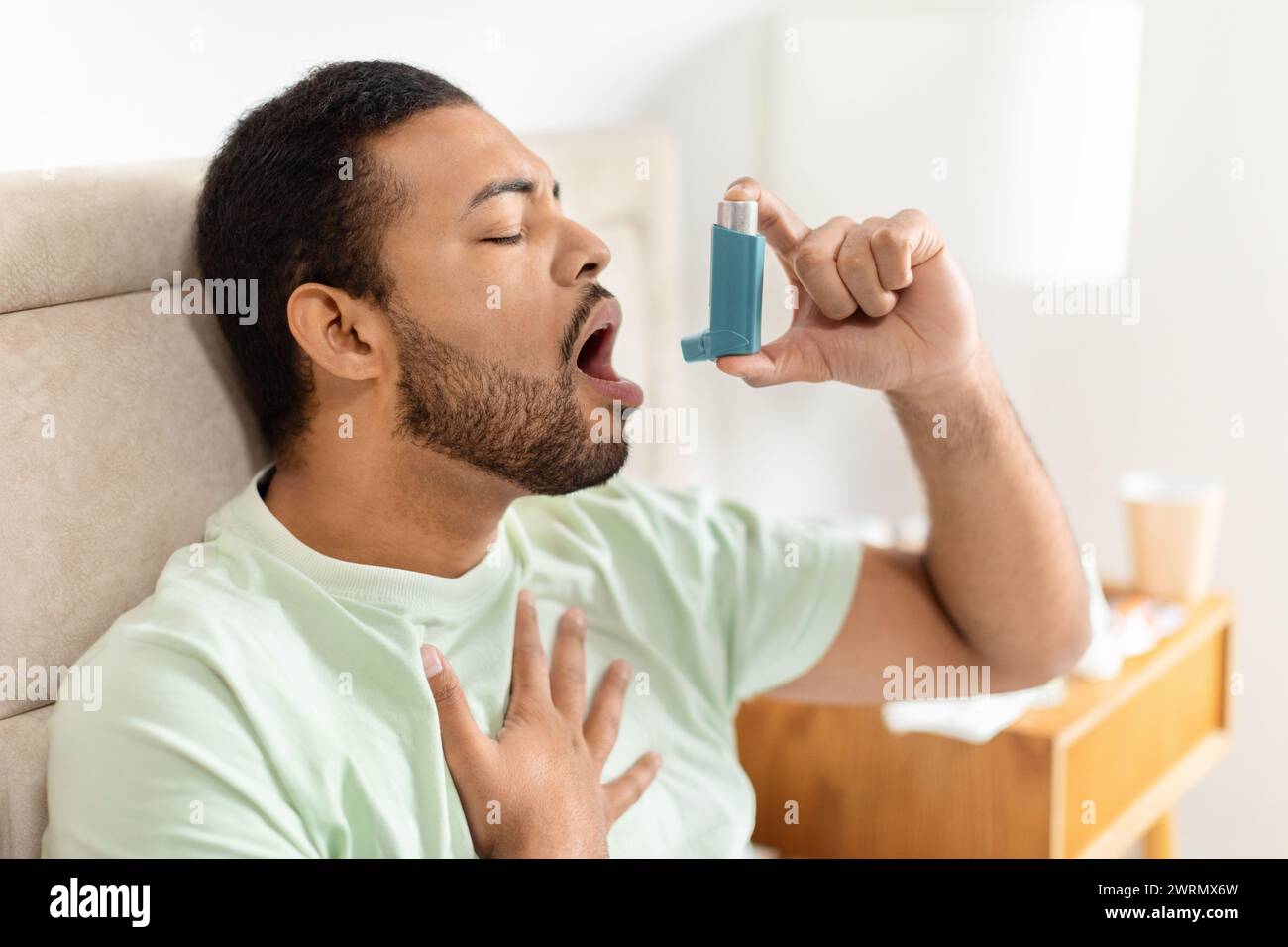 Handsome black man sitting alone at home, using asthma pump Stock Photo ...