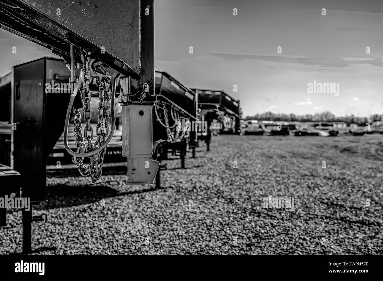 Selective focus on gooseneck trailer hitch with a row of flatbeds lined ...