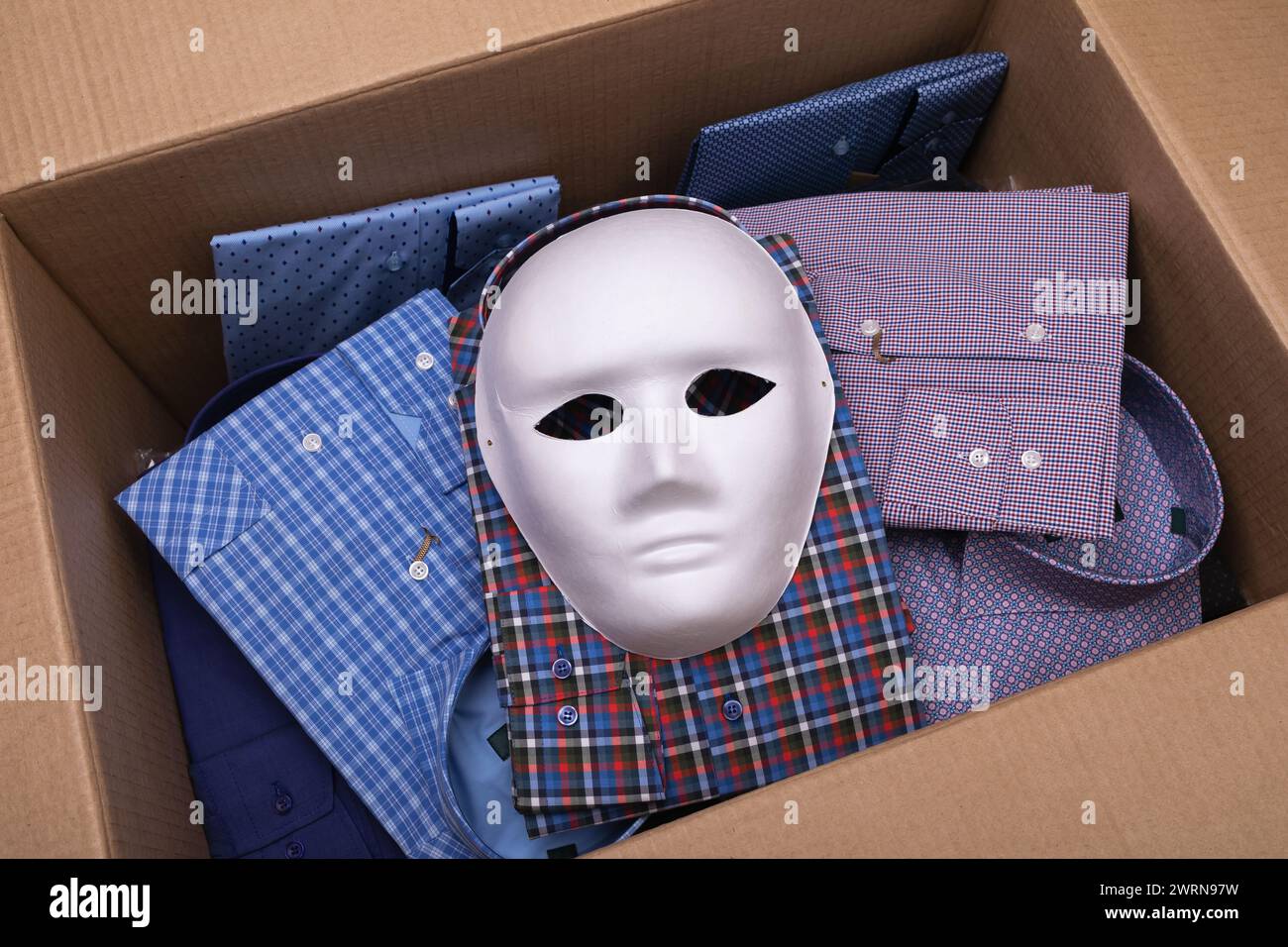 White mask and various shirts in an open cardboard box, concept on the ...