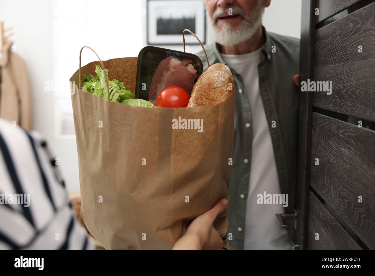 Courier giving paper bag with food products to senior man indoors ...