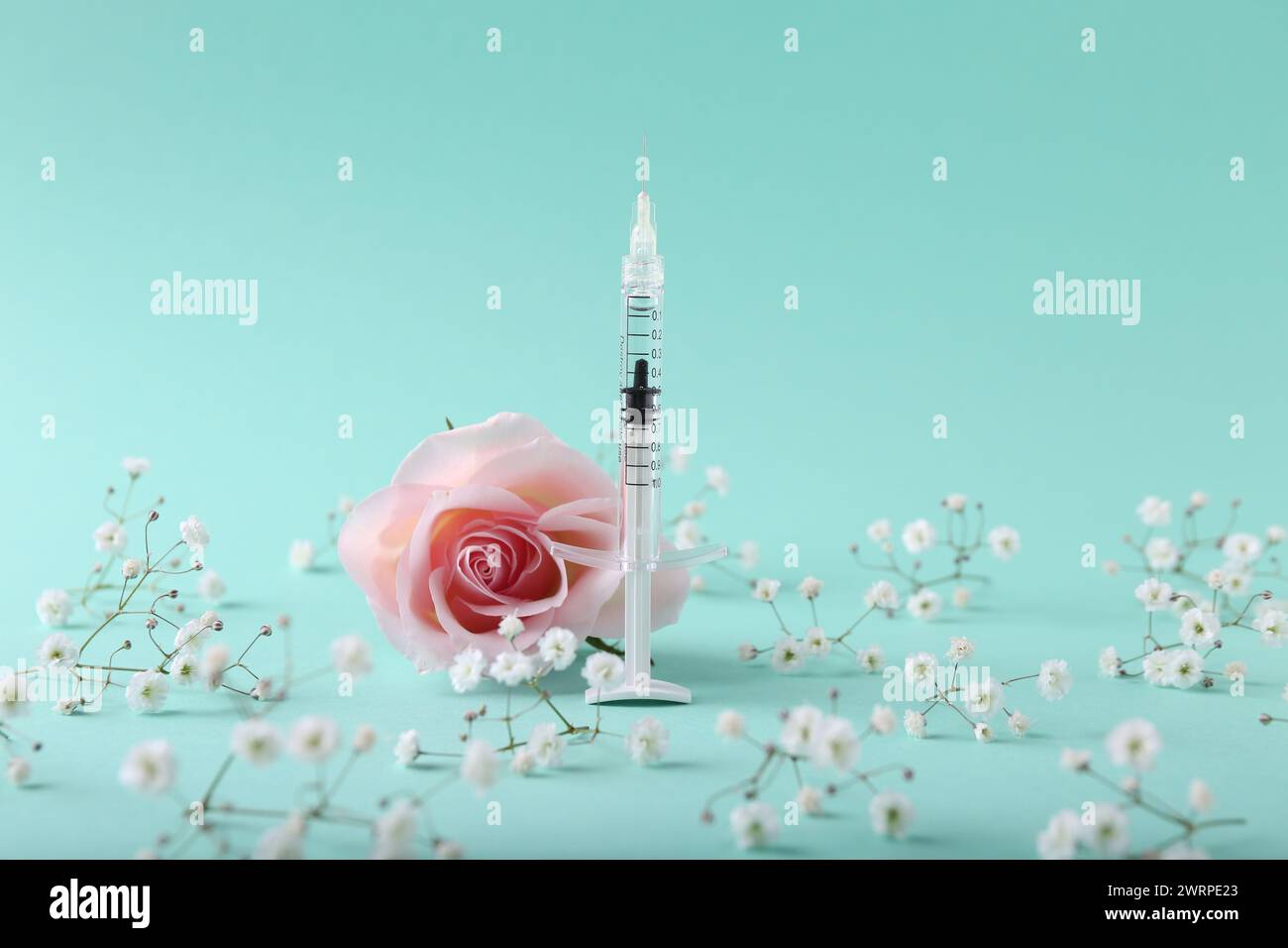 Cosmetology. Medical syringe, rose and gypsophila flowers on turquoise ...