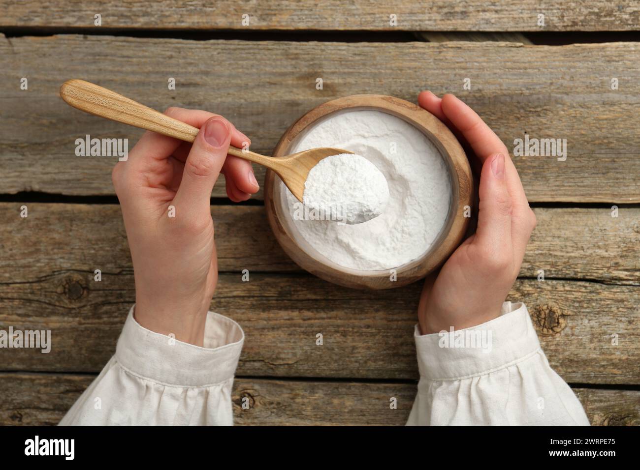 Woman taking baking powder with spoon from bowl at wooden table, top ...