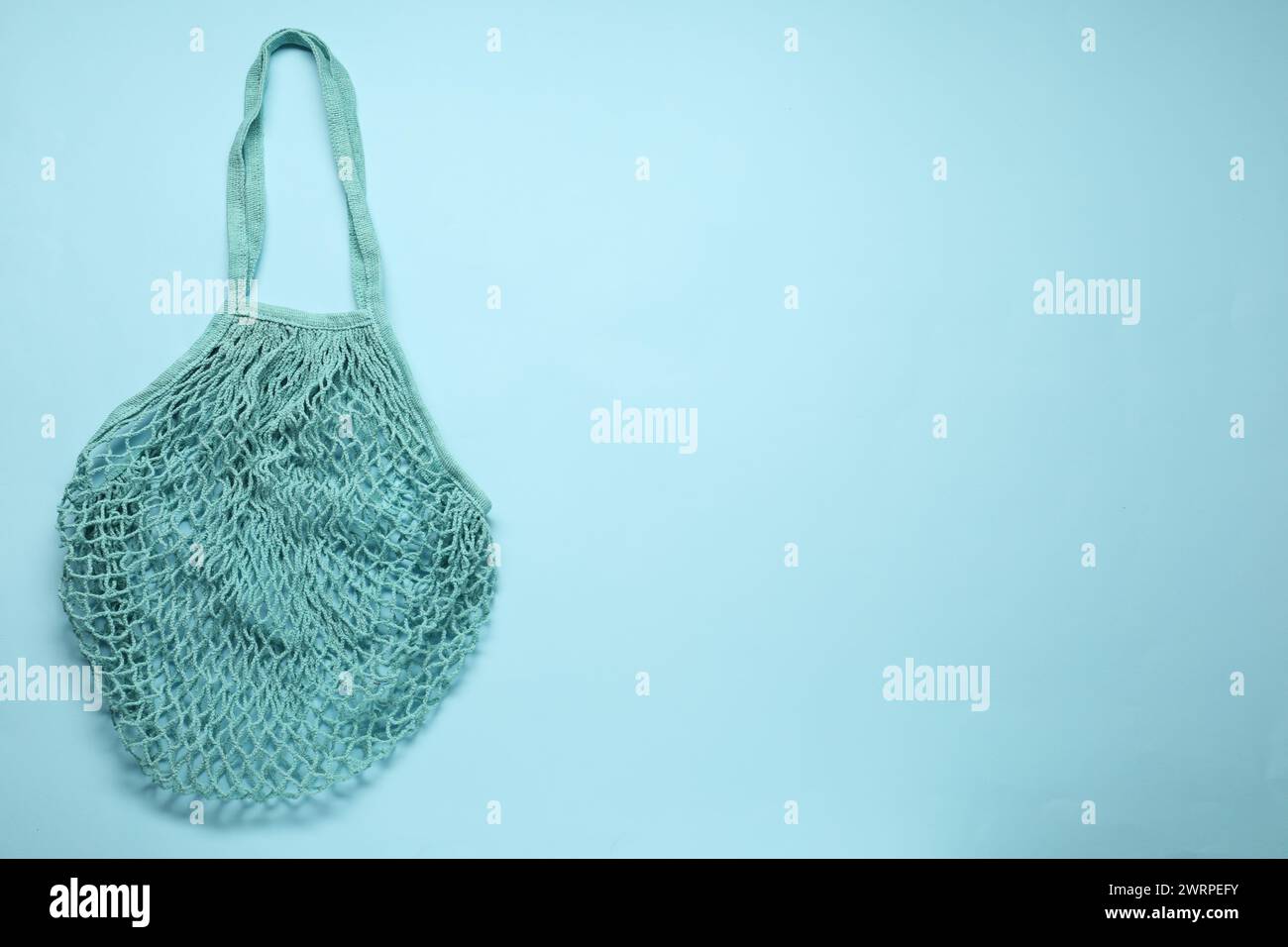 Turquoise net bag on light blue background, top view. Space for text ...