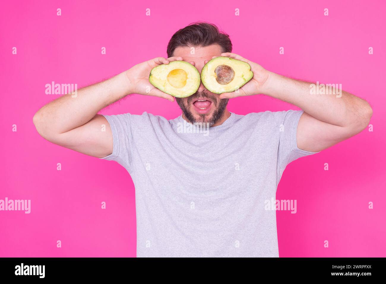 Avocado eyes. Man hold half of fresh avocado isolated on pink ...