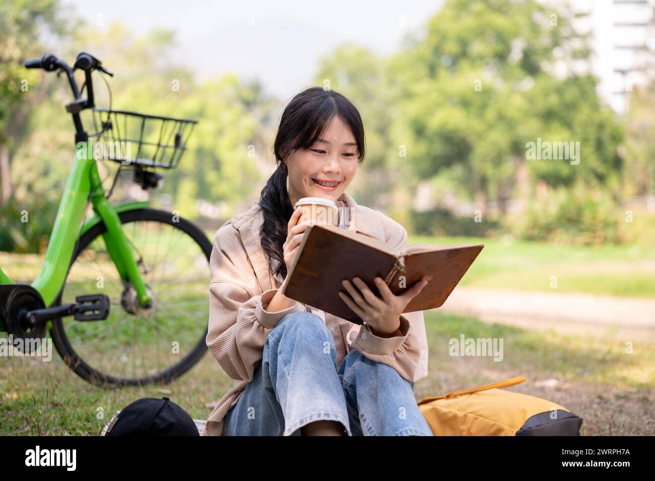A positive, happy young Asian woman is reading a book and sipping ...