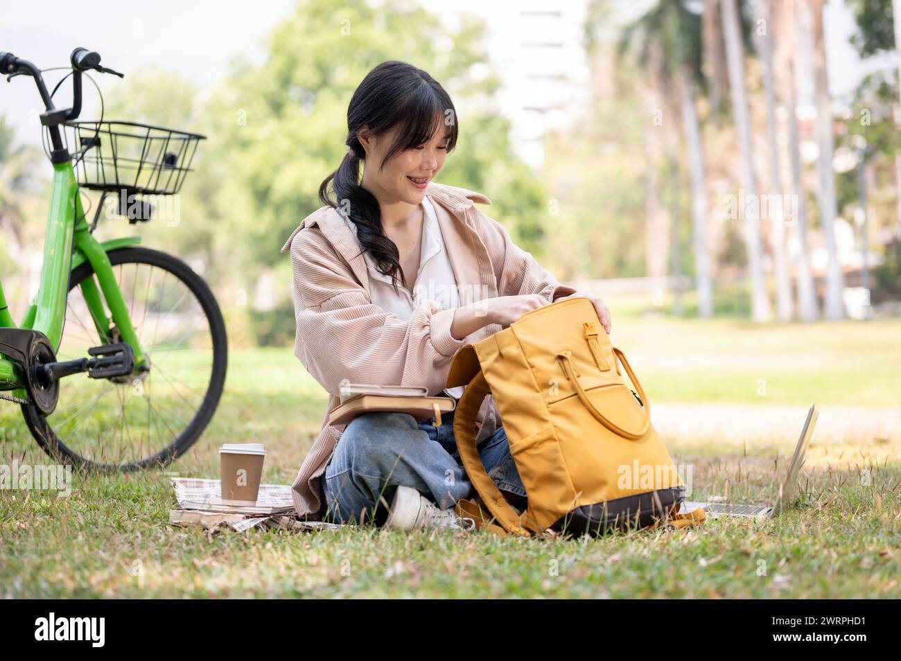 A happy young Asian female college student is chilling in a campus park ...
