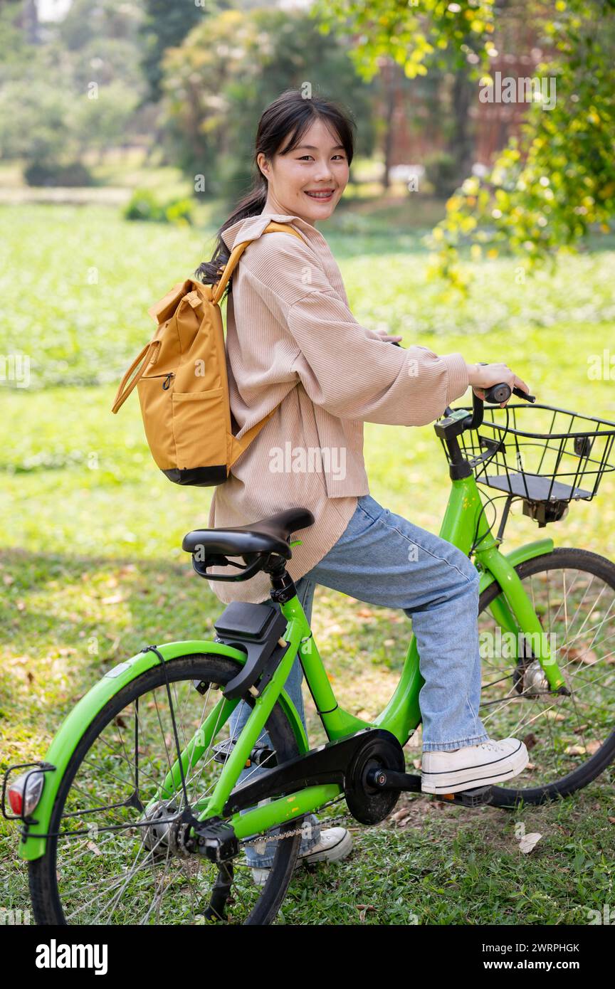 A cheerful young Asian female college student is riding her bike in a ...