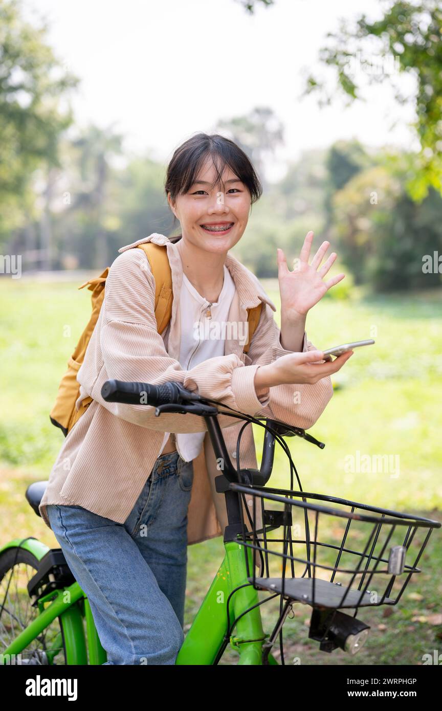A cheerful, smiling young Asian female college student waves her hand ...