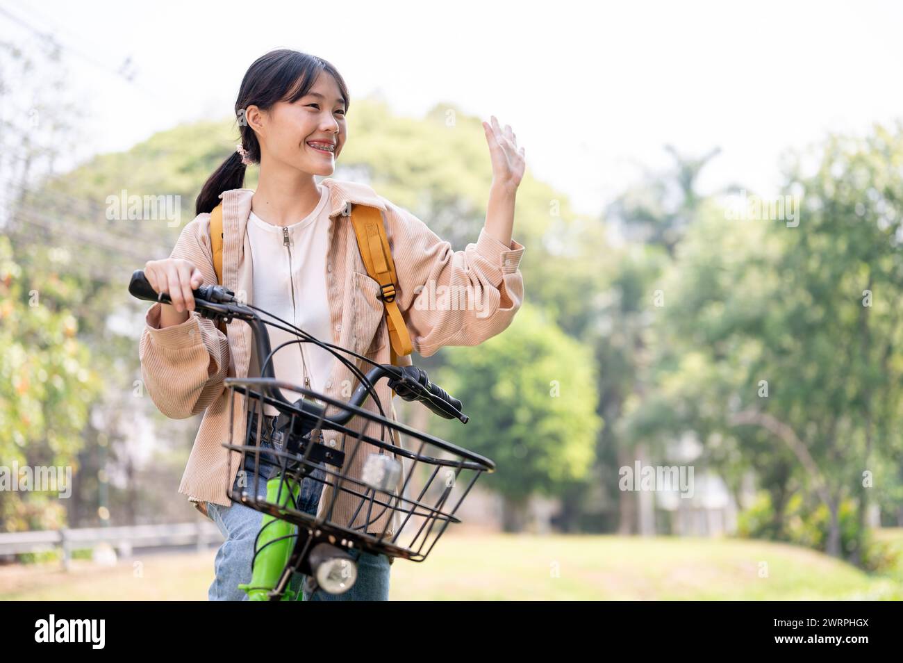 A cheerful, smiling young Asian female college student waves her hand ...