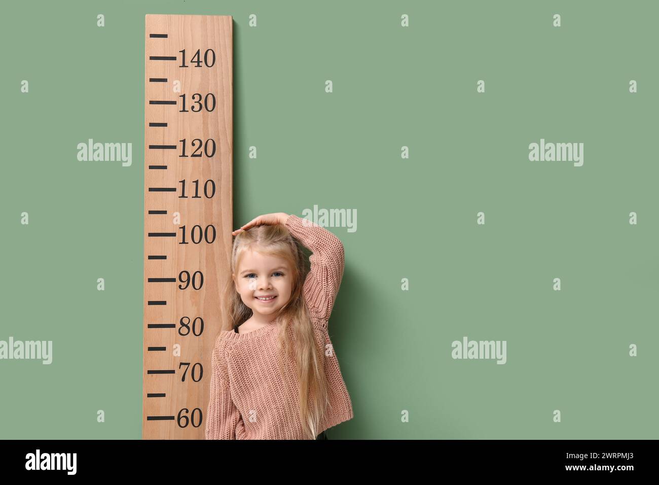 Cute little girl measuring height on green background Stock Photo - Alamy