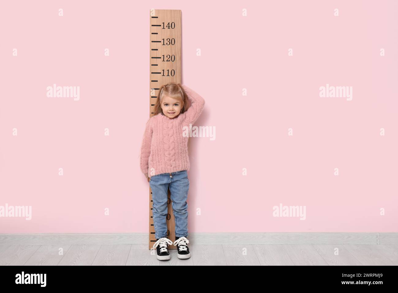 Cute little girl measuring height near pink wall Stock Photo - Alamy