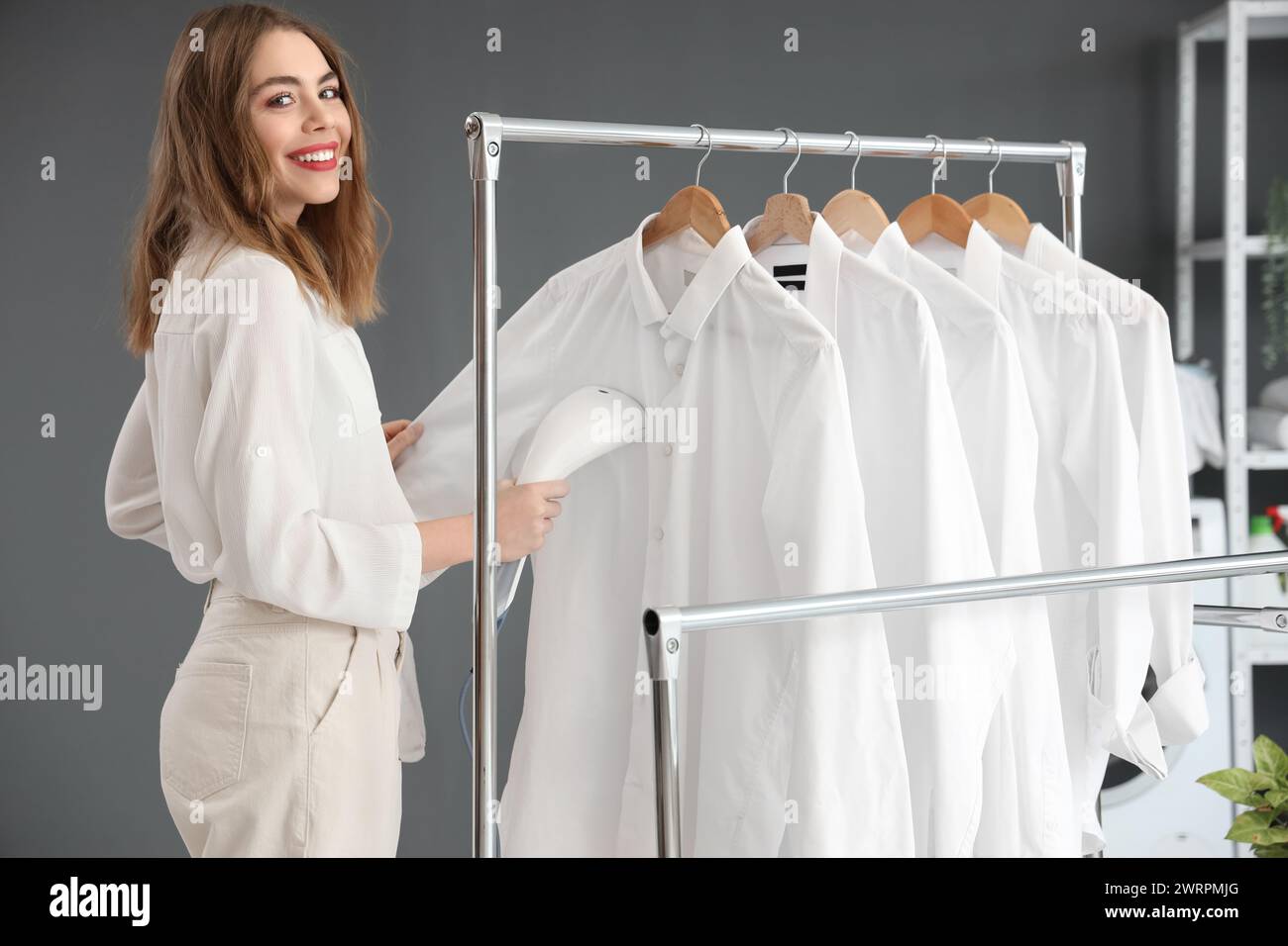 Pretty young woman steaming clothes with modern garment steamer in ...