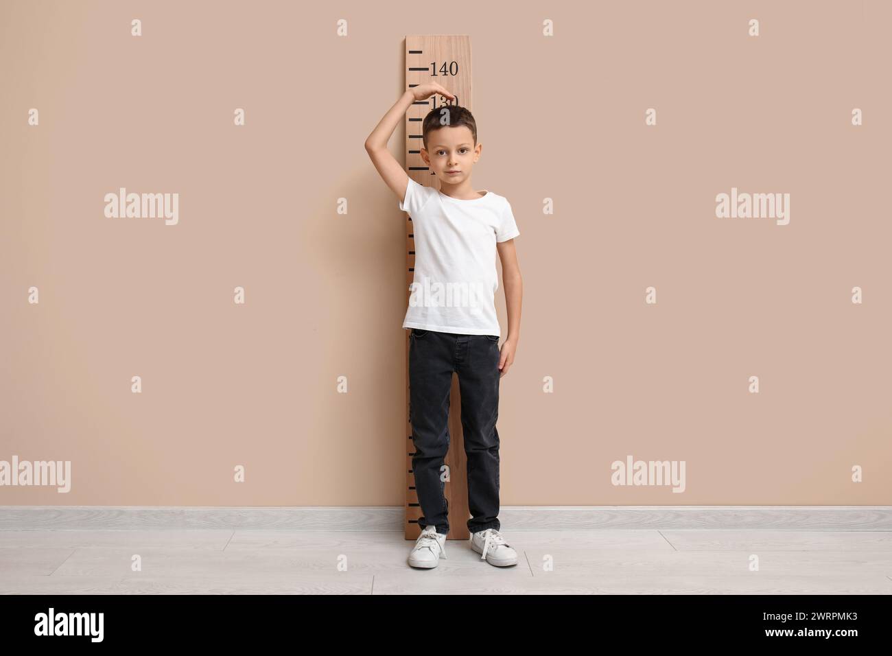 Cute little boy measuring height near beige wall Stock Photo - Alamy