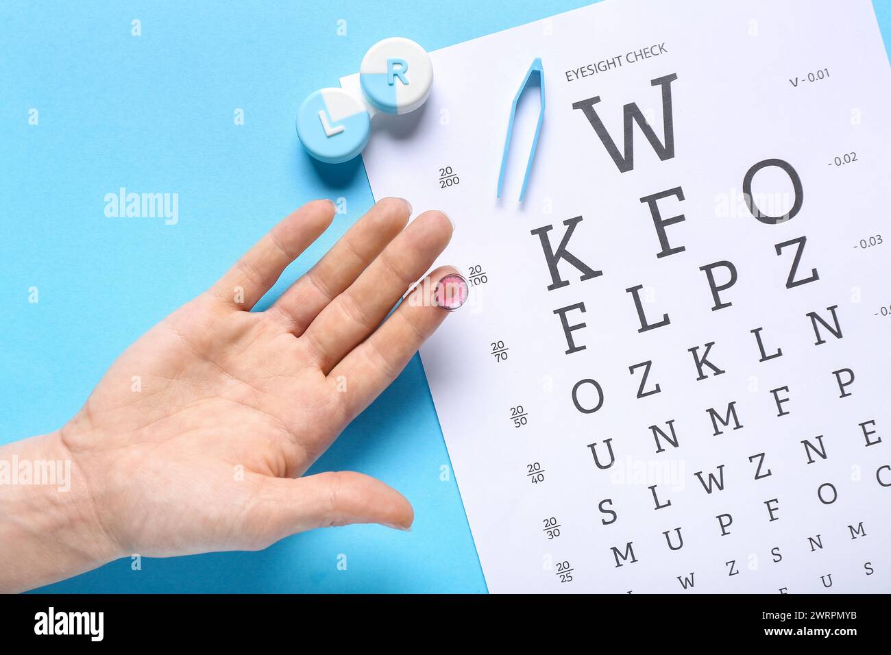 Female hand with contact lens, eye test chart and container on blue ...