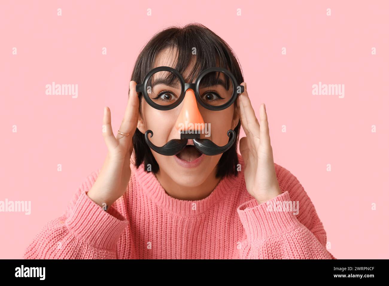 Beautiful young shocked woman in funny disguise on pink background ...