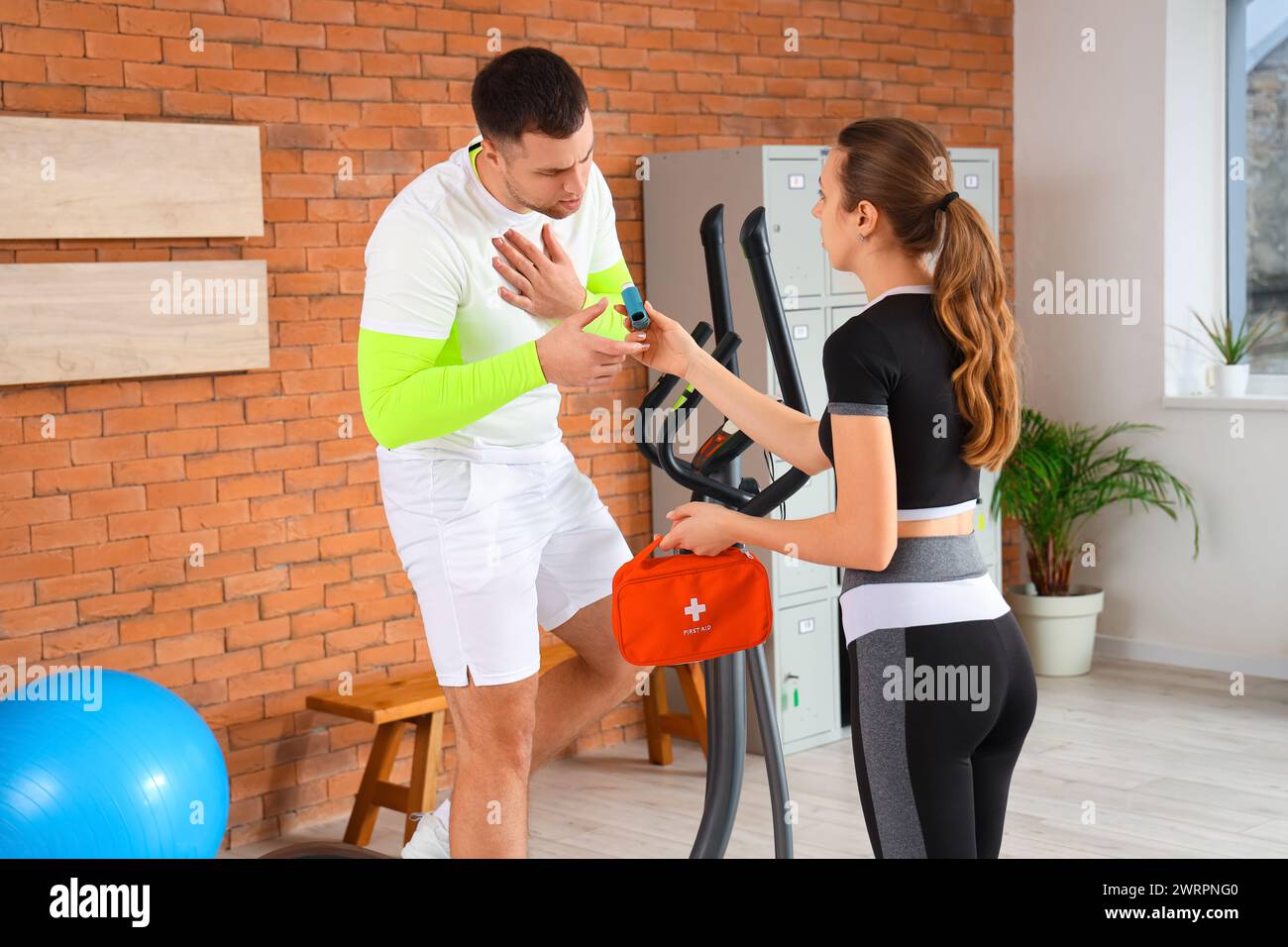 Sporty young man with asthma attack taking inhaler from trainer in gym ...
