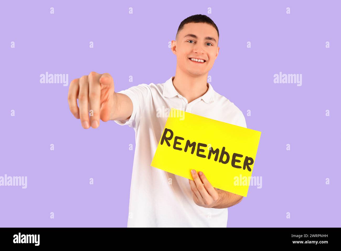 Young man holding paper with word REMEMBER and pointing at viewer on ...