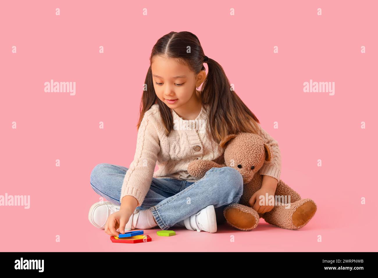 Little Asian girl with autistic disorder playing on pink background ...