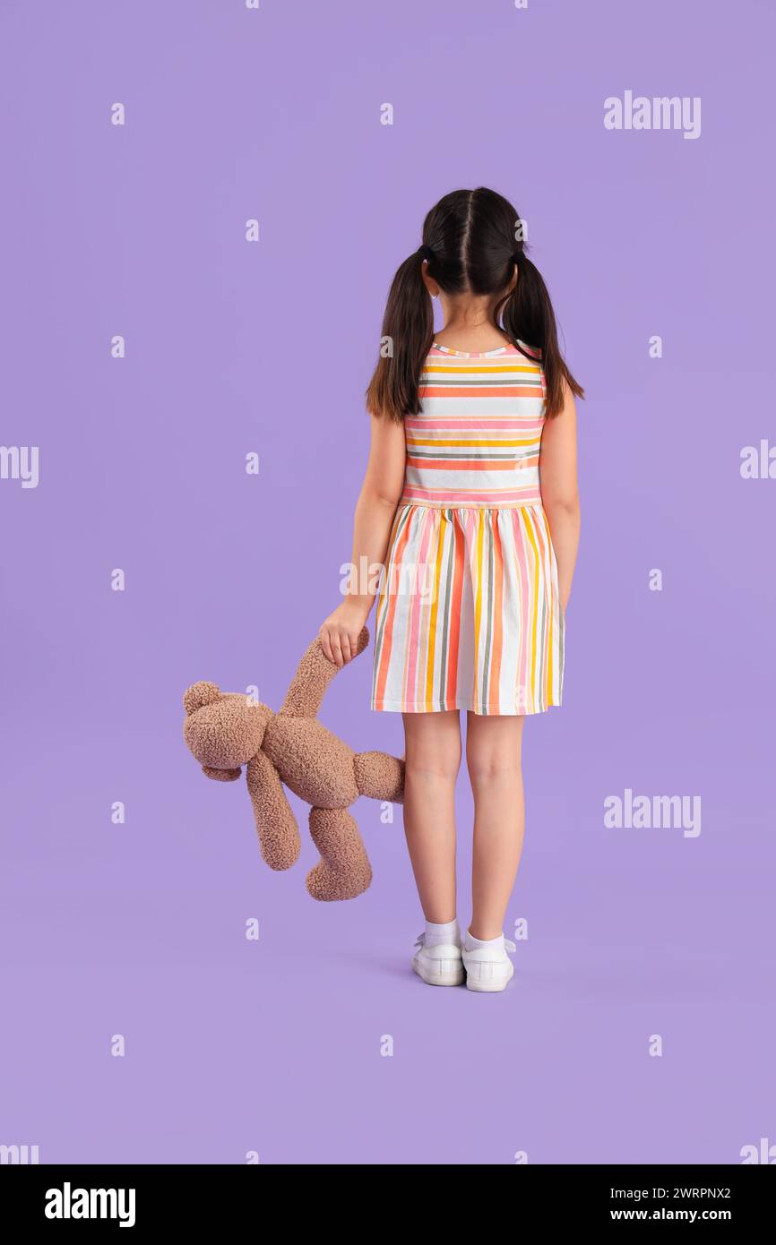 Little girl with autistic disorder and toy bear on lilac background ...
