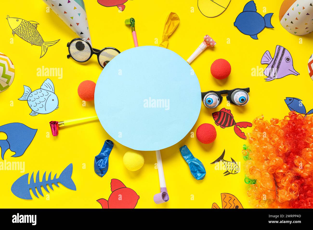 Blank card with paper fishes, clown wig and party decor on yellow ...