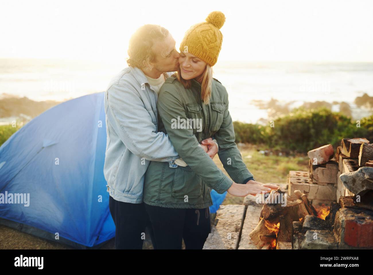 Happy couple, kiss and bonding together by campfire, outdoor and romantic getaway with camping ...
