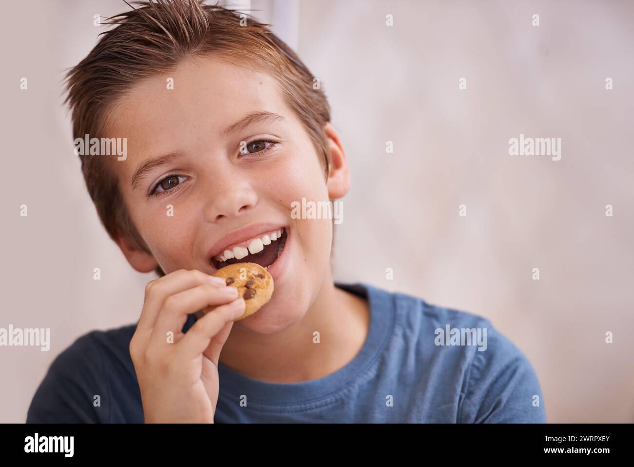 Portrait, smile and boy eating cookie in kitchen of home for hunger ...