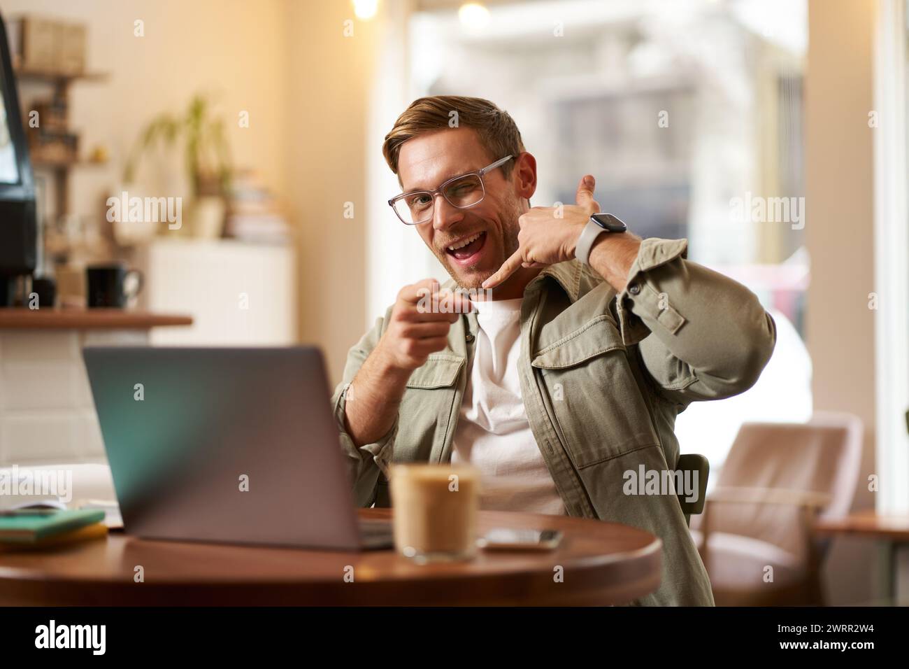 Portrait of cheerful, flirty guy in glasses, sitting with laptop ...