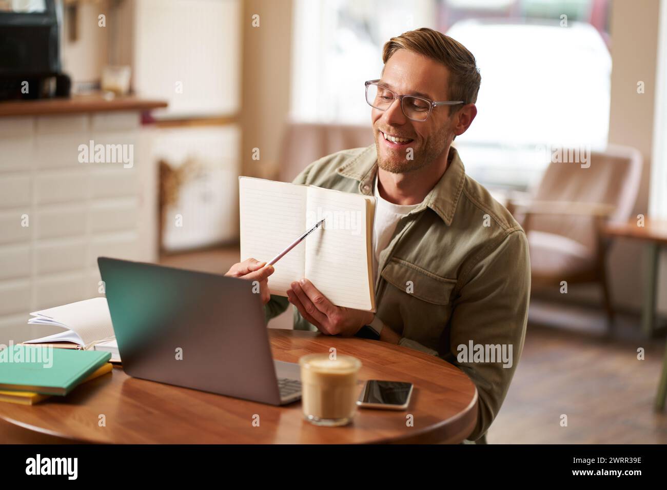 Portrait of handsome man in glasses, working remotely from empty cafe, showing example in his ...