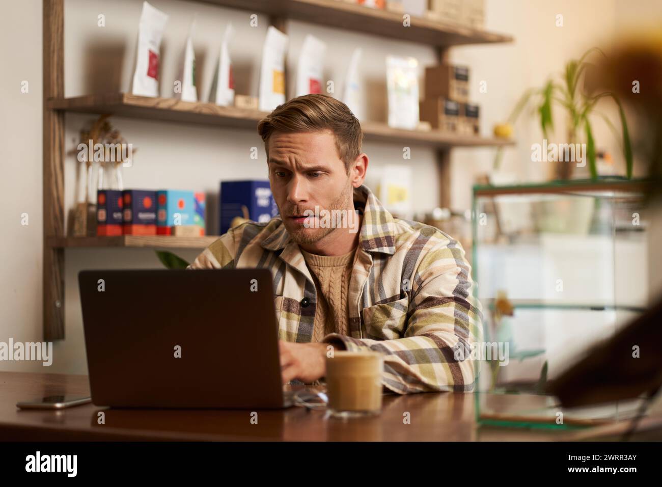 Image of young business owner, man sitting in cafe with laptop, looking ...