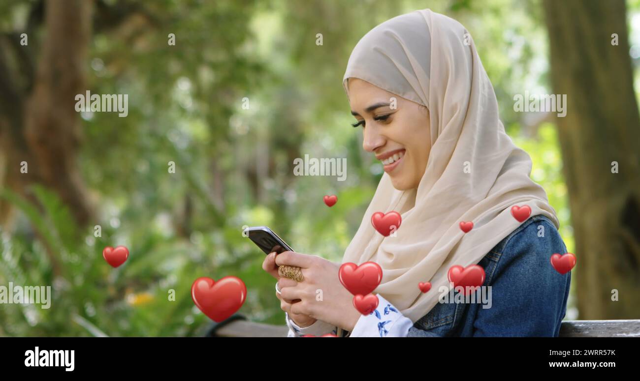 Muslim woman in hijab texts with hearts flying around her on a bench in ...