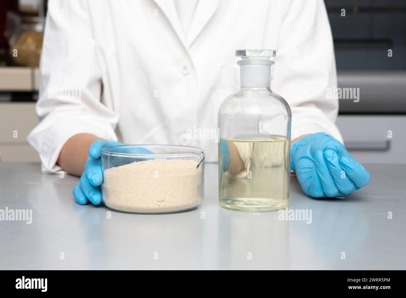 A scientist's gloved hands conducting an experiment with clear liquid chemicals and a solid ...
