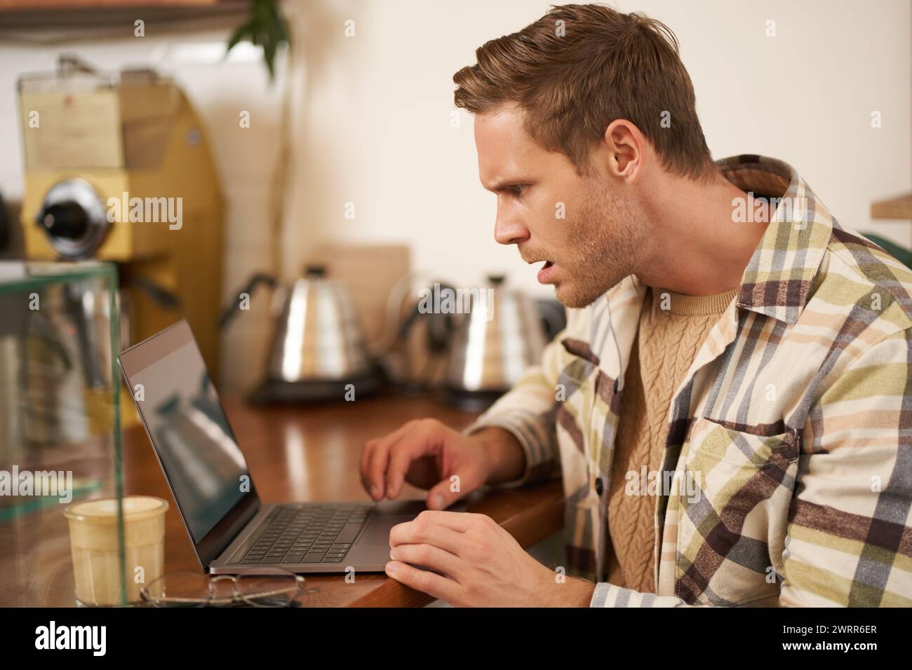 Portrait of man looks frustrated at laptop screen, staring at monitor ...