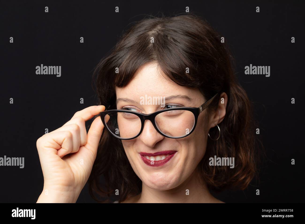 Charming young woman playfully adjusting her black framed glasses Stock Photo - Alamy