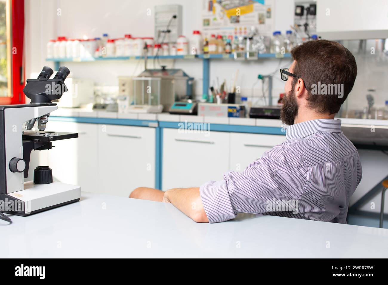 A male scientist in a striped shirt sits thoughtfully in a lab ...