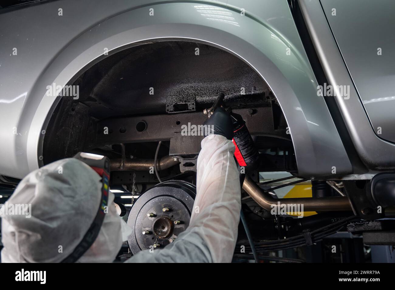 An auto mechanic applies anti-corrosion mastic to the underbody of a ...